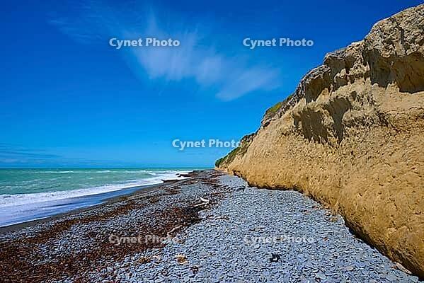 Cliff with pebble beach and blue sky on a sunny day, Tuhawaiki Point ...