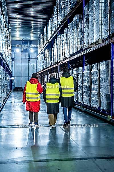 Workers wearing safety vests walking down an aisle in a cold storage ...