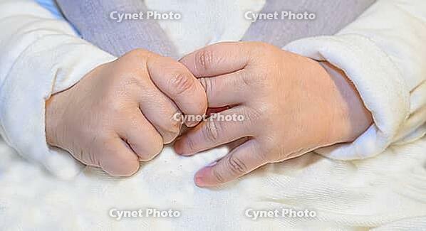 Close-up of relaxed baby hands against soft white clothing, conveying ...